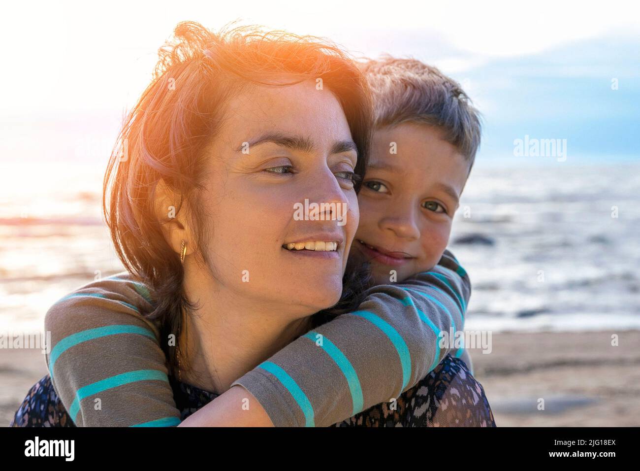 Cute happy boy hugs his mom on the seashore in the sunset light Stock ...
