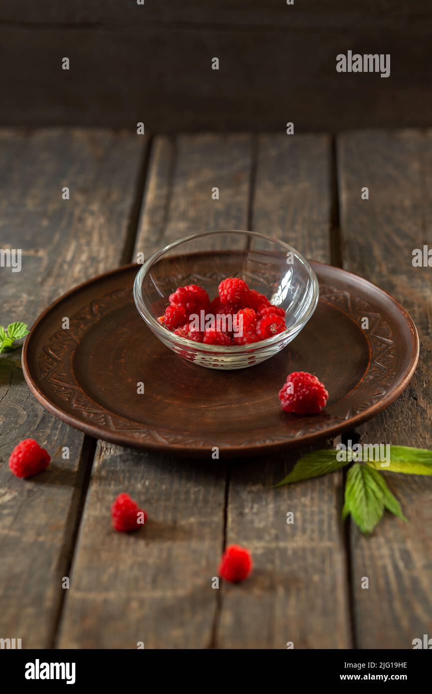 raspberries in a transparent saucer on a ceramic plate on wooden boards ...