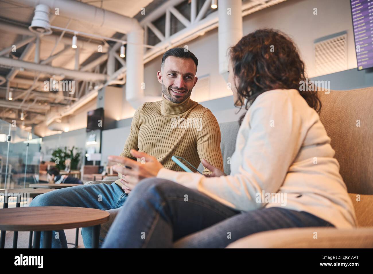 Happy young Caucasian couple talking while sitting in VIP lounge of an airport departure ...