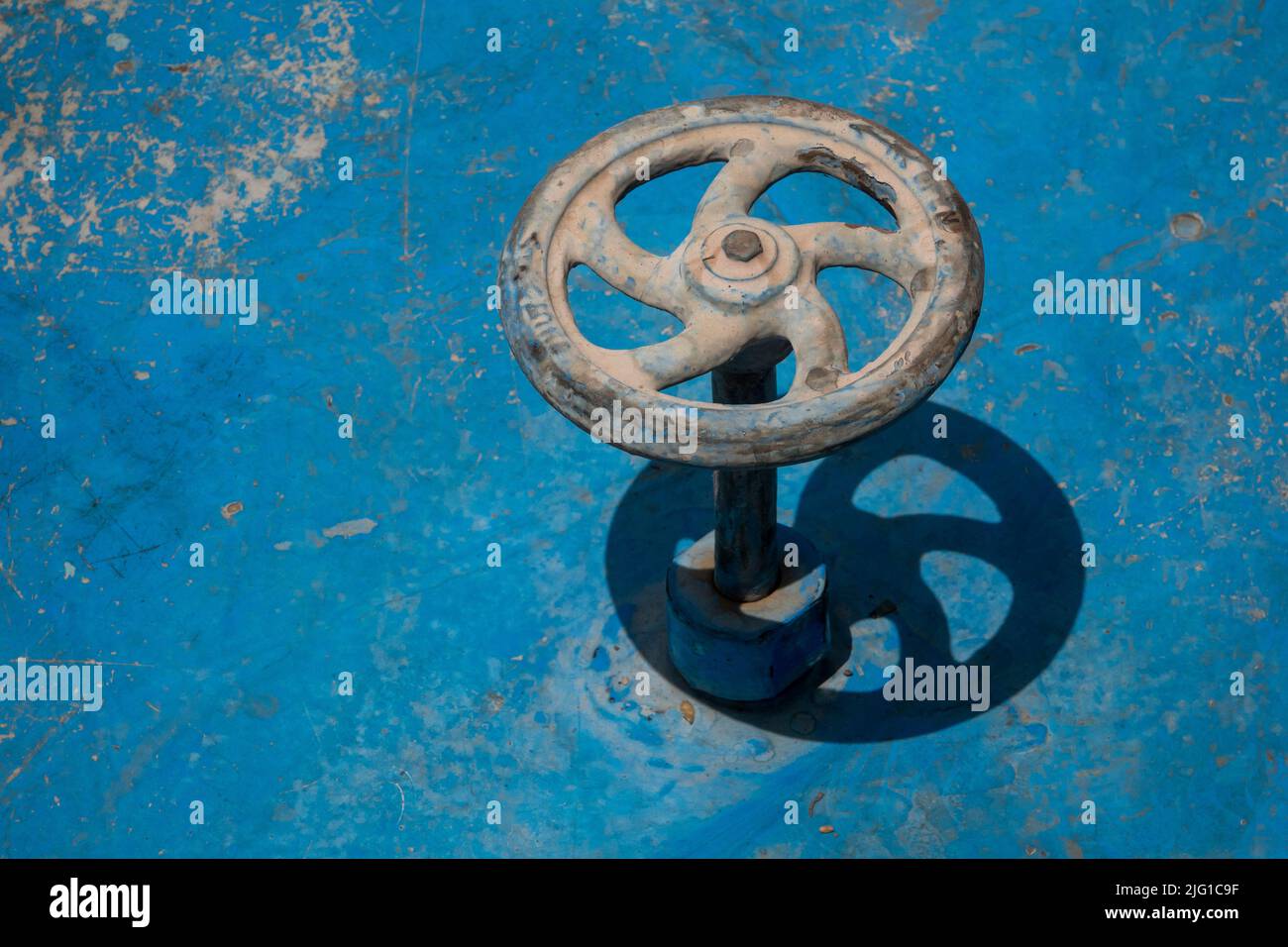 Valve wheel with strong shadow protruding from a blue painted ship's ...