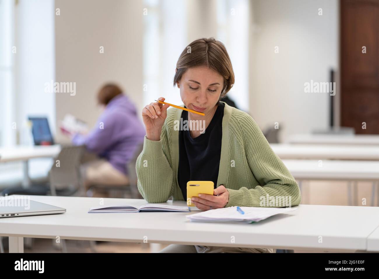 Focused pensive middle-aged woman using mobile app while studying ...