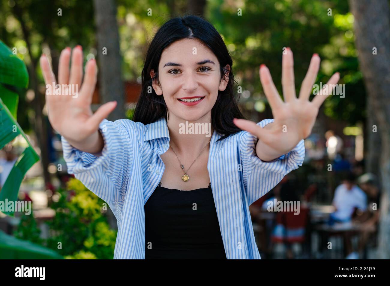 Cheerful Brunette Woman Wearing Blue Striped Shirt On City Park Outdoors Showing And Pointing