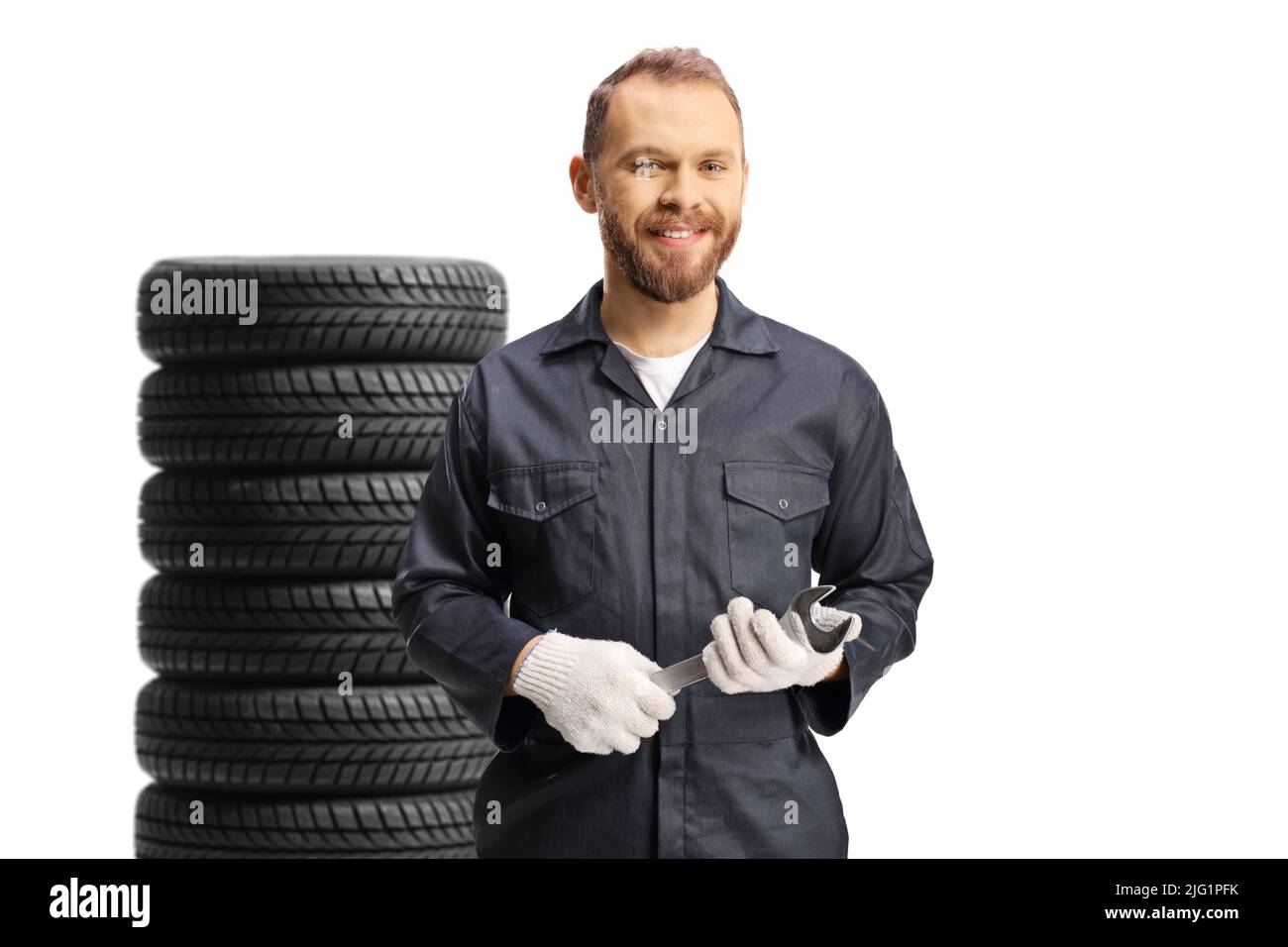 Smiling mechanic in a uniform with tires holding a wrench tool isolated ...