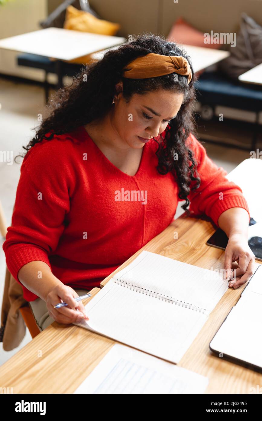 Focused biracial mid adult businesswoman reading note pad at desk in ...