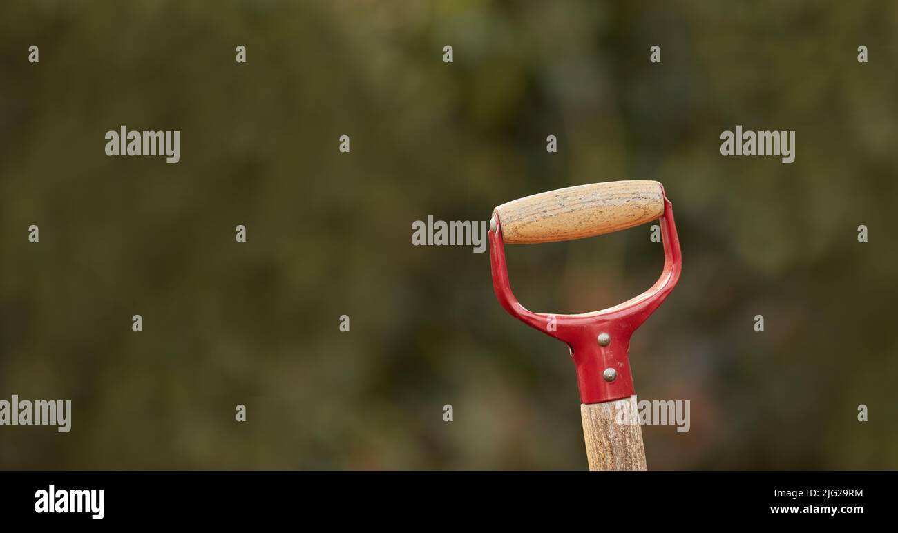 Closeup of a shovel handle in a garden outside against a blur ...