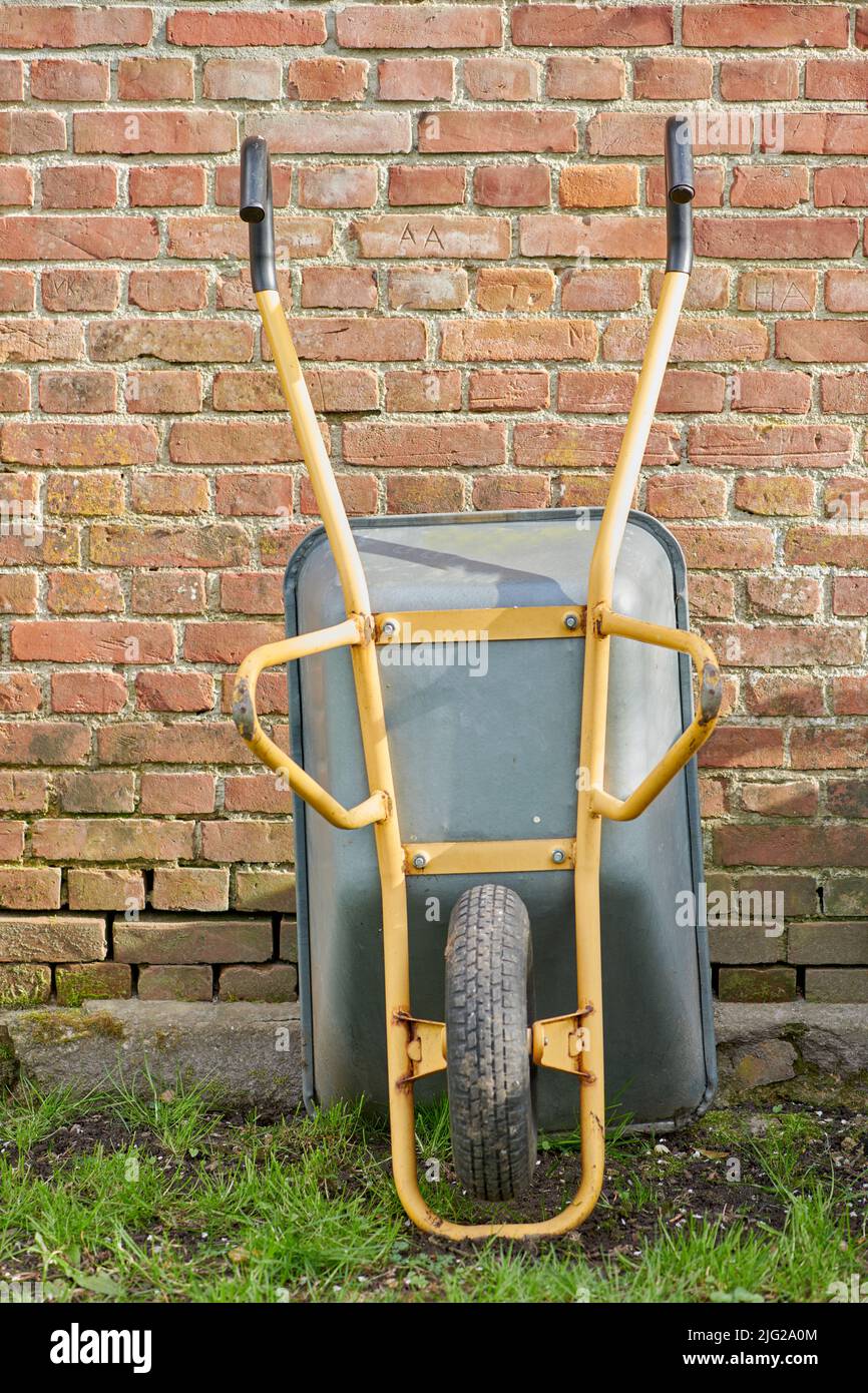 Garden wheelbarrow leaning against a red brick wall in a home backyard ...