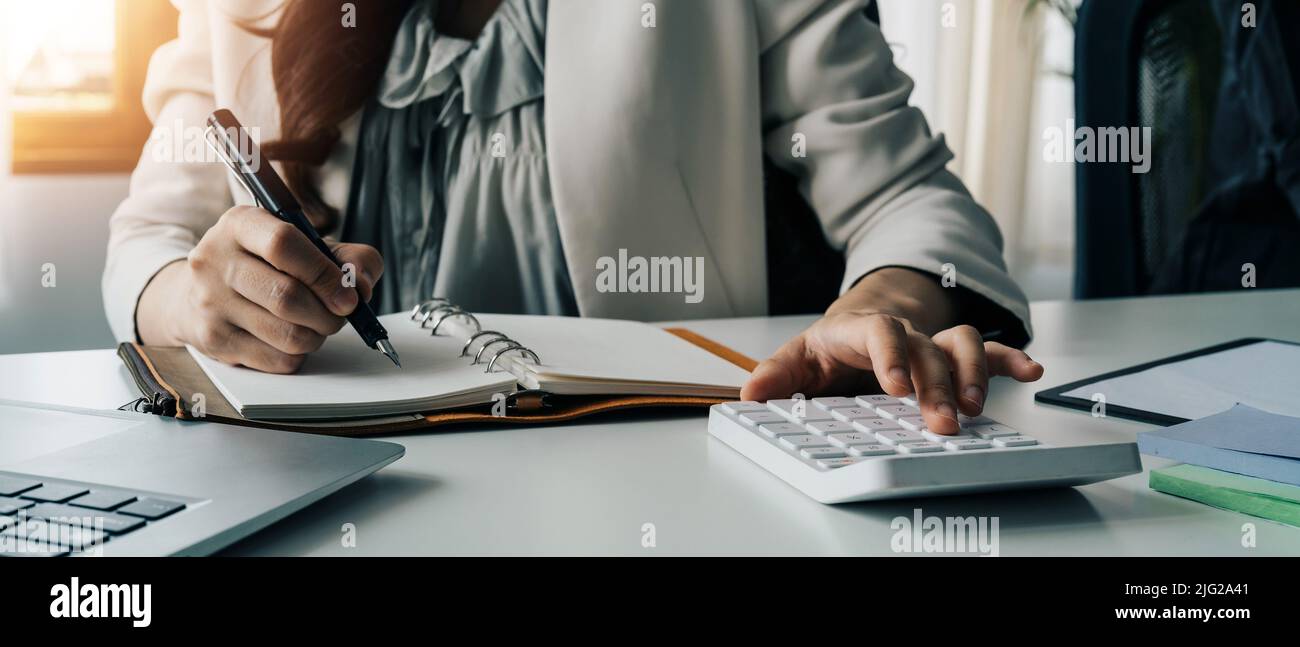Accountant female writing information on paper while using calculator ...