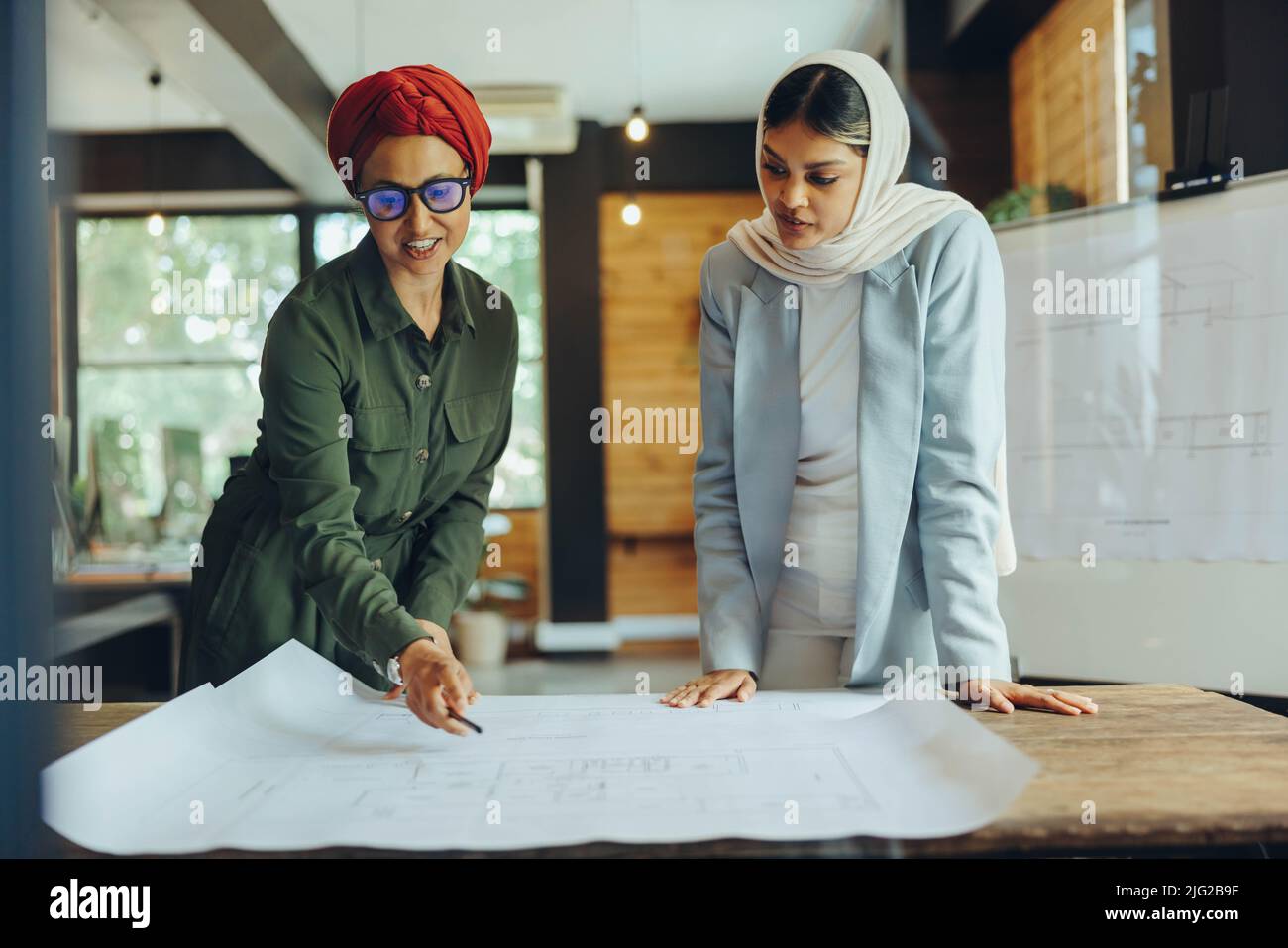 Muslim architects working on blueprint drawings in a modern office. Two creative businesswomen ...