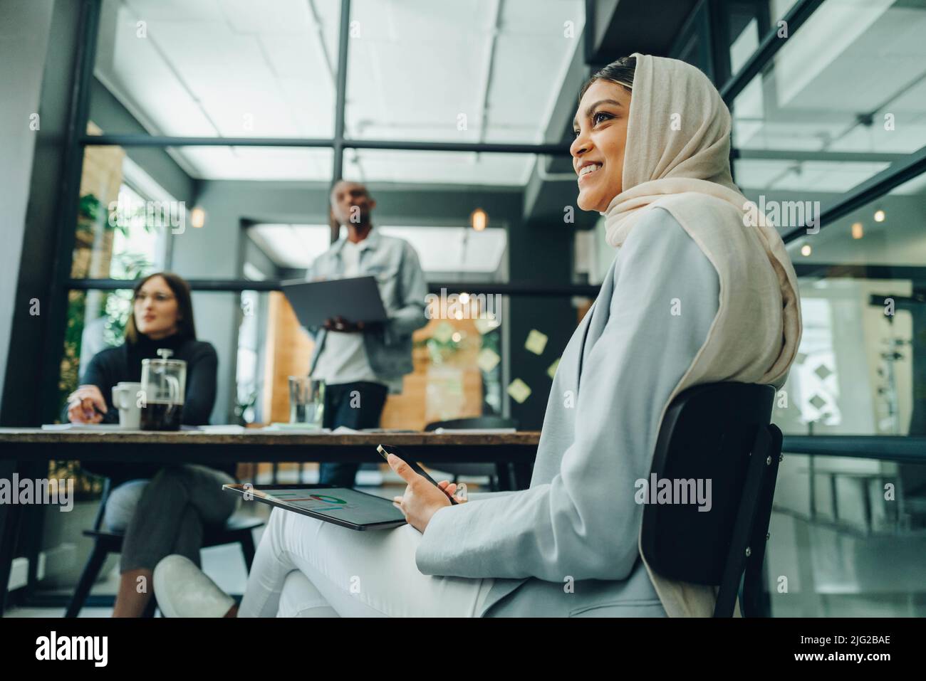Happy Muslim businesswoman holding wireless technology while sitting in ...
