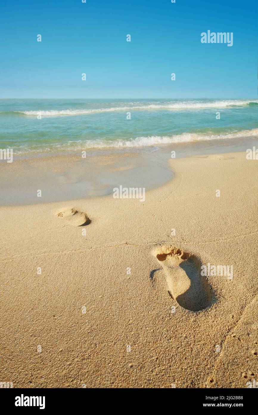 Footsteps on a sand beach seaside with a white foamy wave from the blue ...