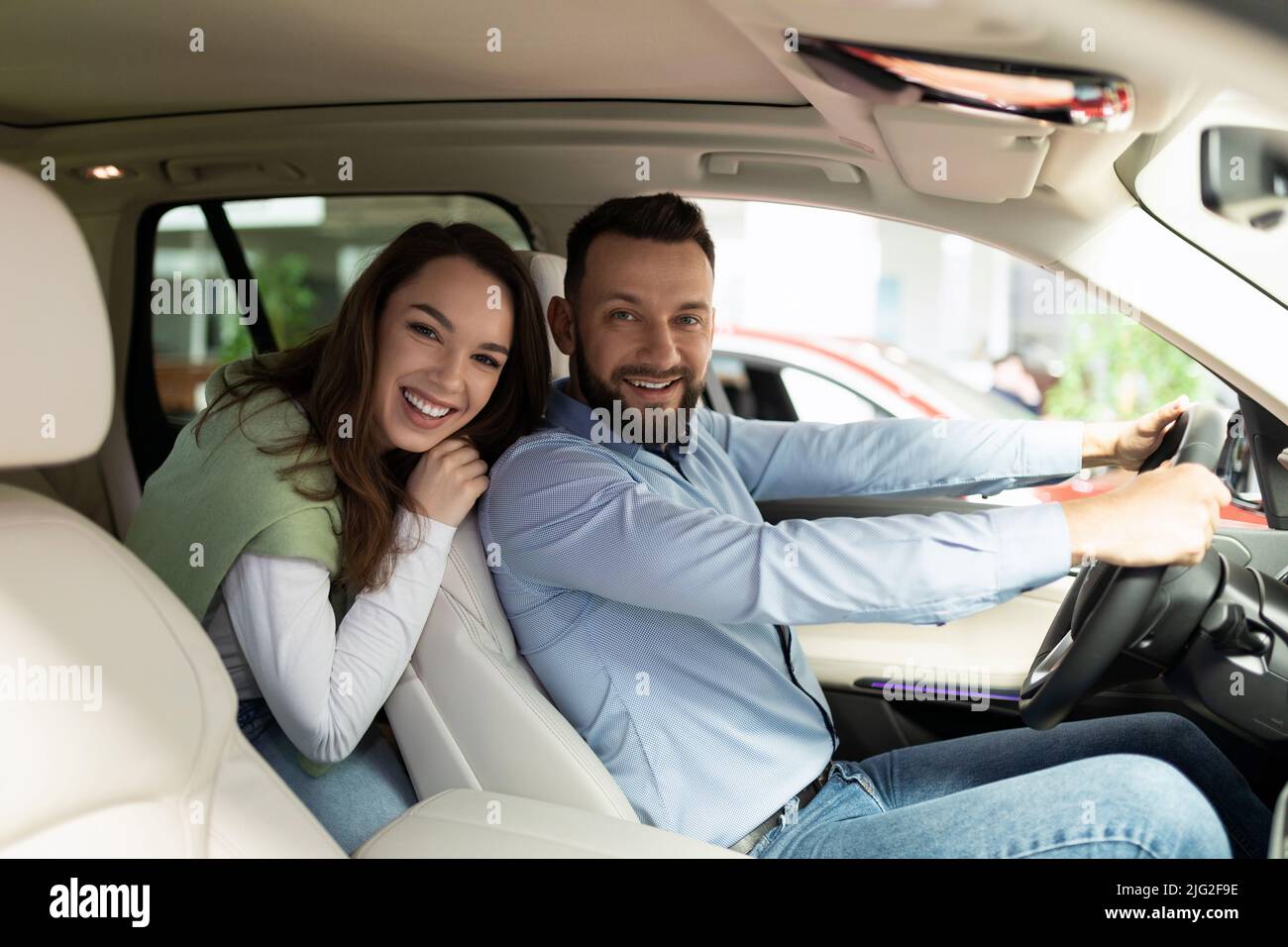 happy young couple driving their new car at a car dealership looking at ...