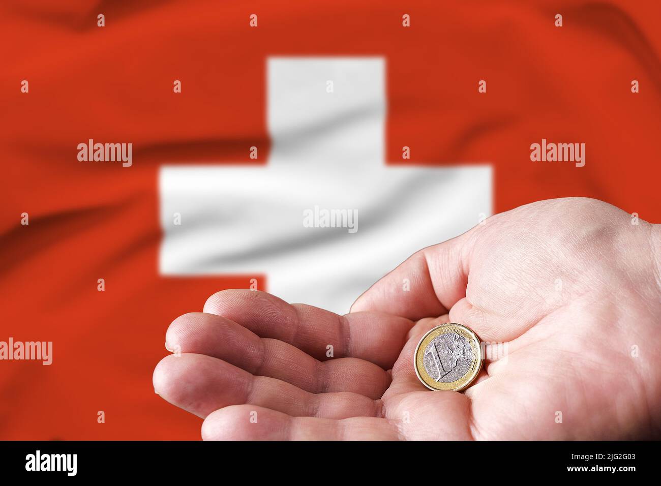 Coin one euro in the hand of a man, the flag of Switzerland on the ...