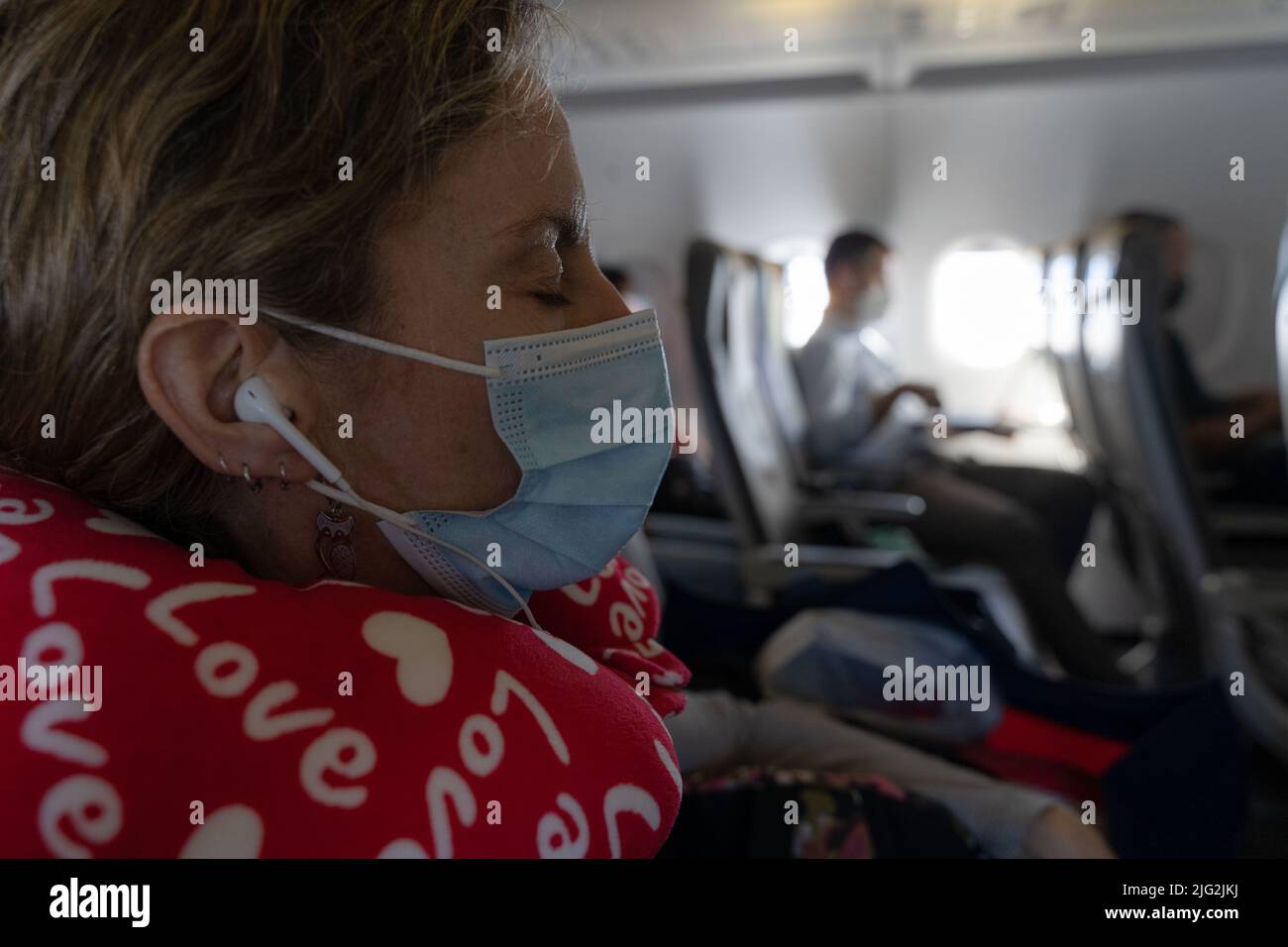 Woman with face mask, earphones and neck pillow sleeping on plane ...
