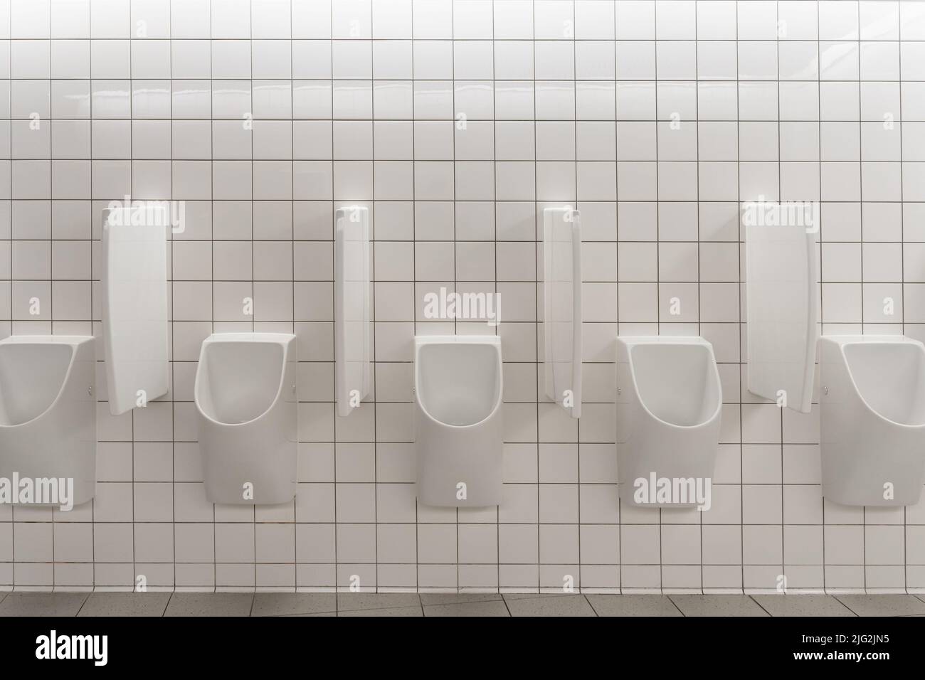 Front view of white urinals on tiled wall. Interior of public restrooms ...