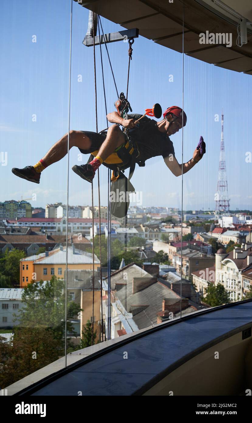 Industrial mountaineering worker hanging on climbing rope and cleaning ...