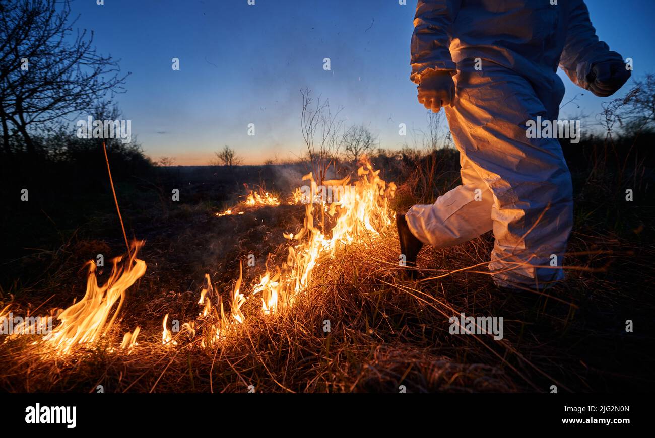 Fireman ecologist fighting fire in field at night. Cropped view of man ...