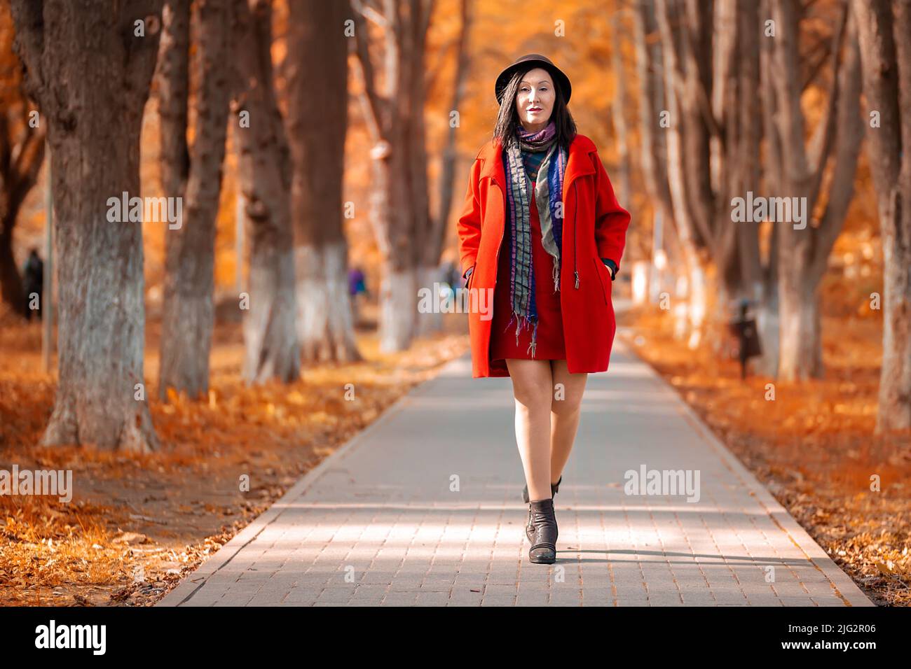 Elegant beautiful adult woman in a red coat and hat walks along the ...