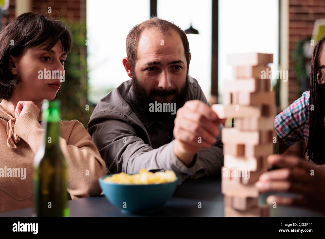 Focused man pulling wood block from tower structure while playing ...