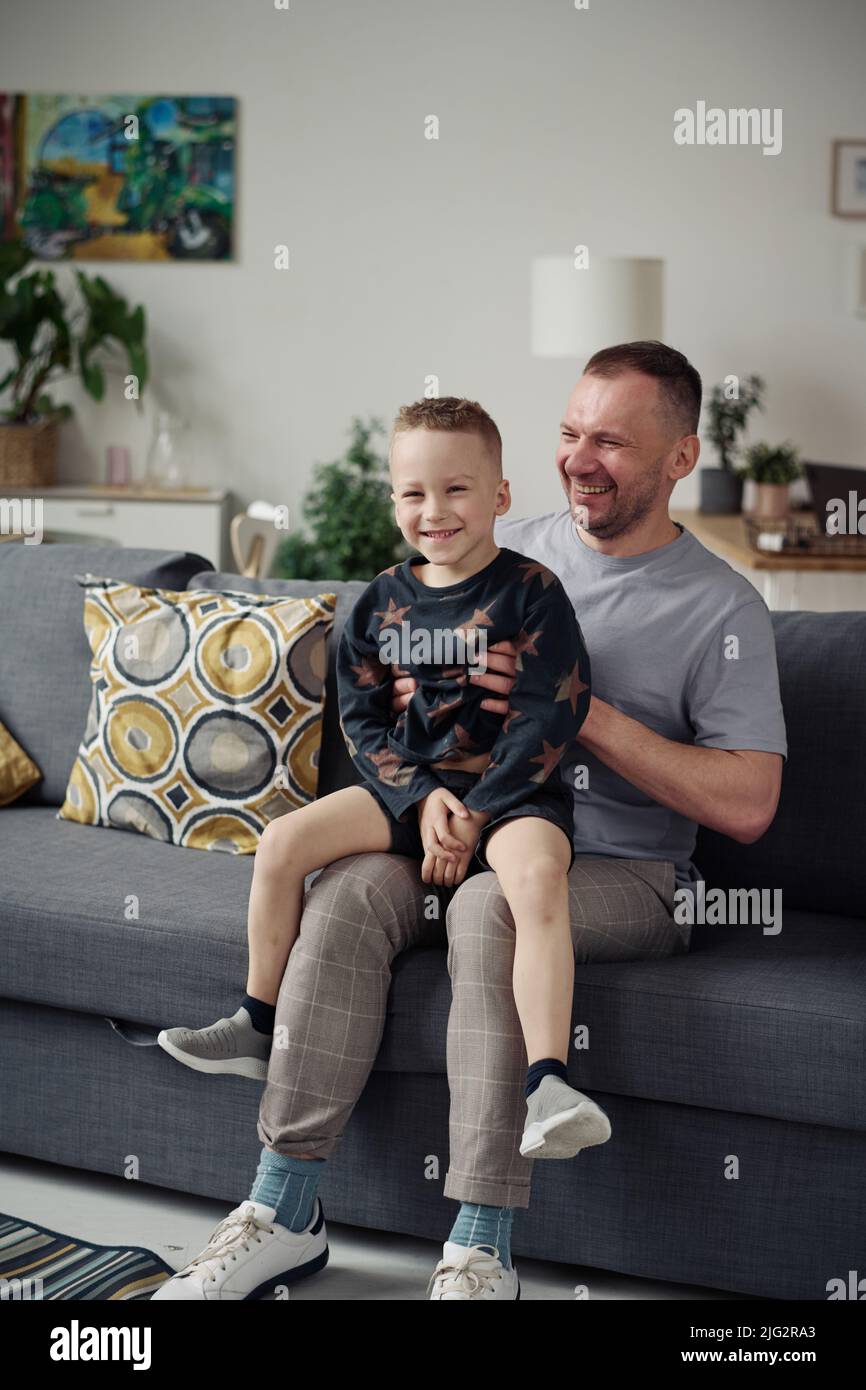 Happy little boy sitting on knees of his dad and playing with him on ...