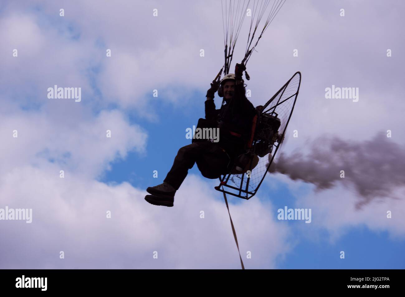 Parachute pilot flying with engine at a cloudy weather with smoke at ...