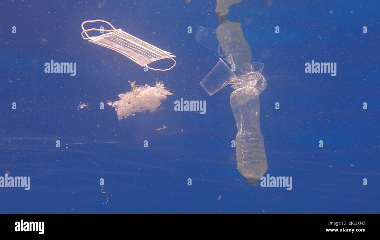 Plastic bottle, cups and medical face mask swim in the blue water ...