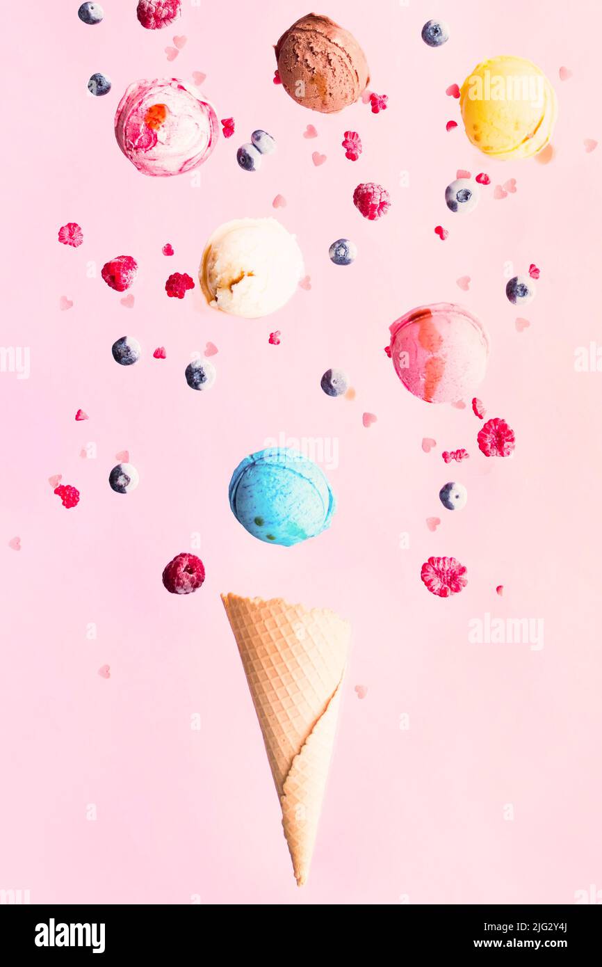 Falling ice cream scoops and berries into the vafel cone on pink ...