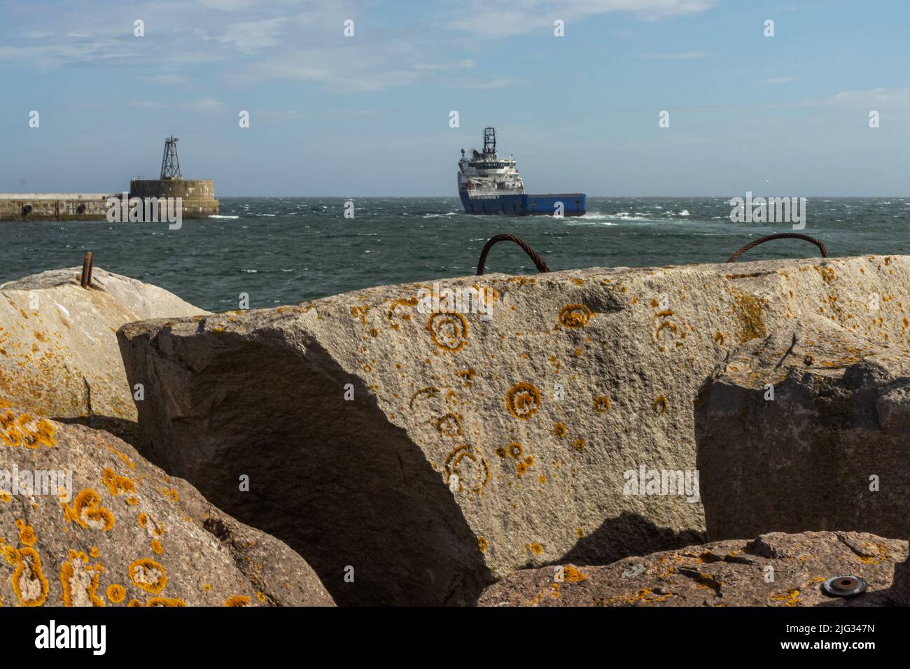 A blue and white cargo ship leaving Peterhead Harbour, with breakwater ...
