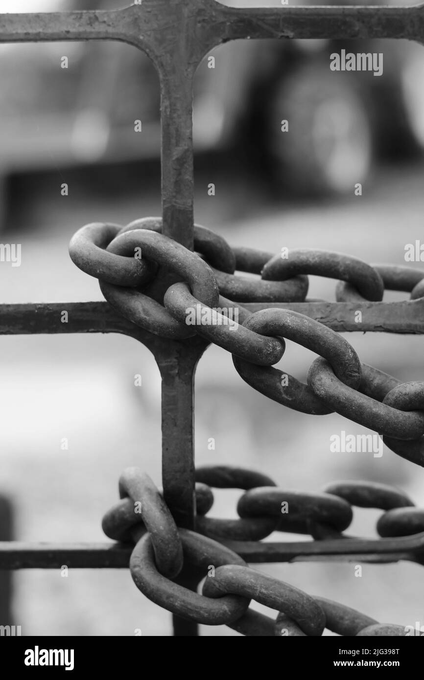Heavy duty industrial metal chain hanging on a fence in black and white ...