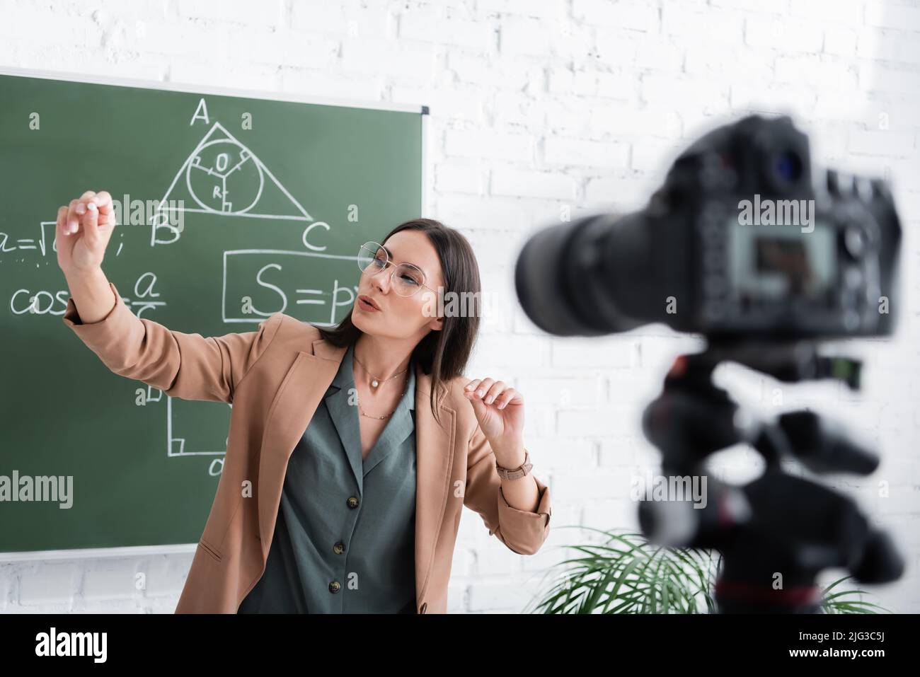 Teacher in eyeglasses talking near chalkboard with mathematic formulas ...