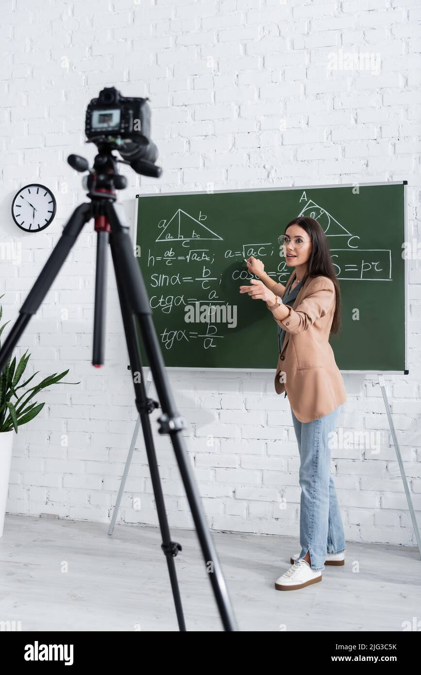 Teacher writing math formula on chalkboard near digital camera in class ...