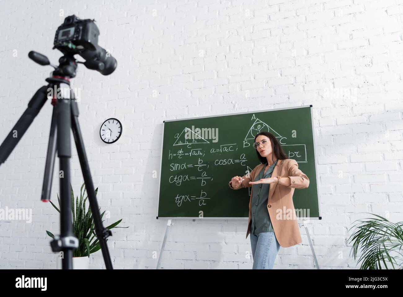 Teacher gesturing near chalkboard with math formulas and digital camera ...