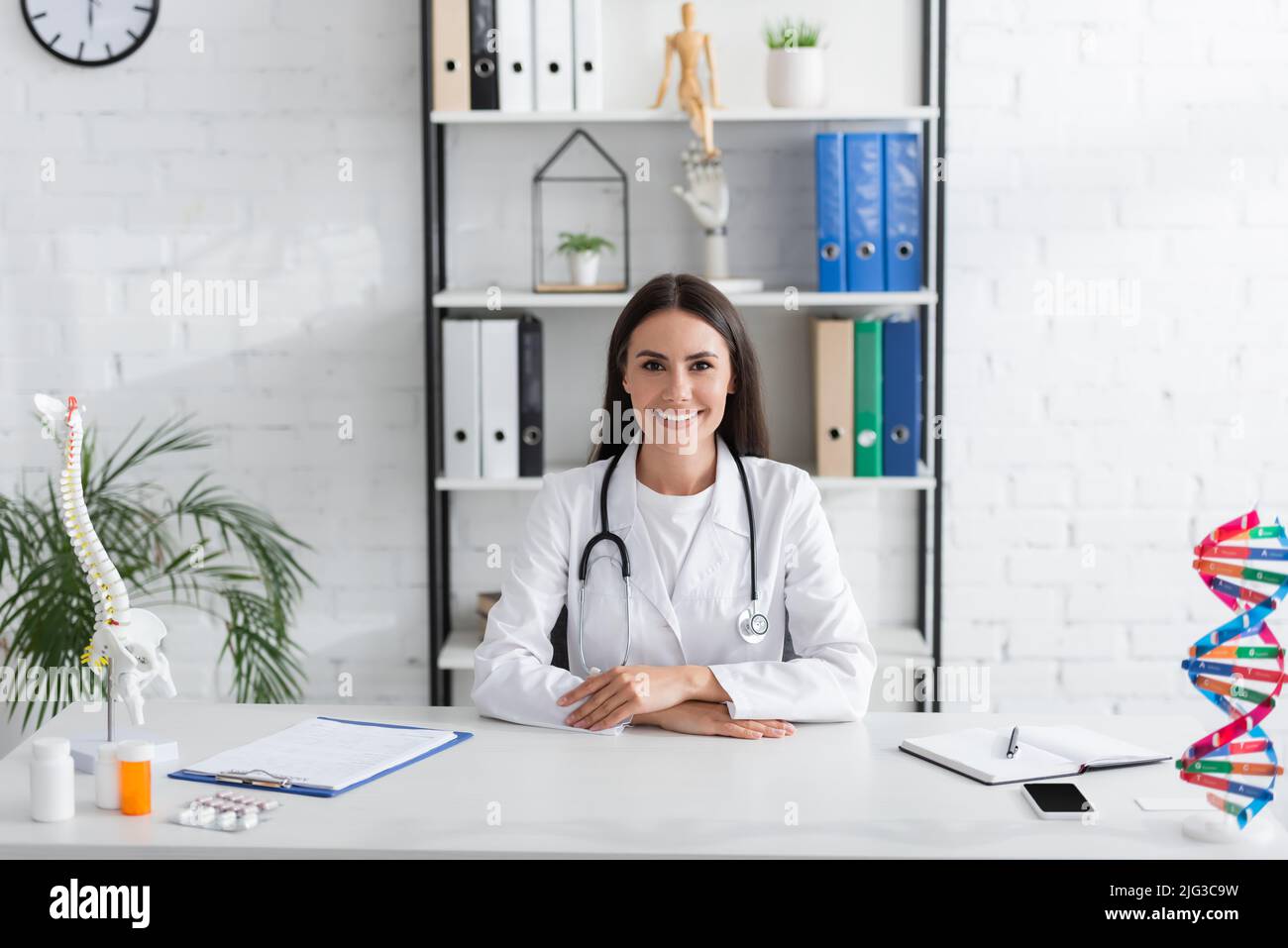 Smiling doctor looking at camera near dna and spinal models and ...