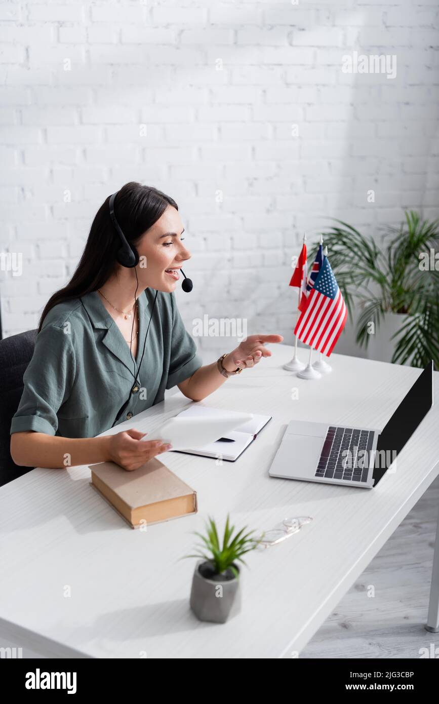 Side view of smiling teacher in headset talking during video call on ...