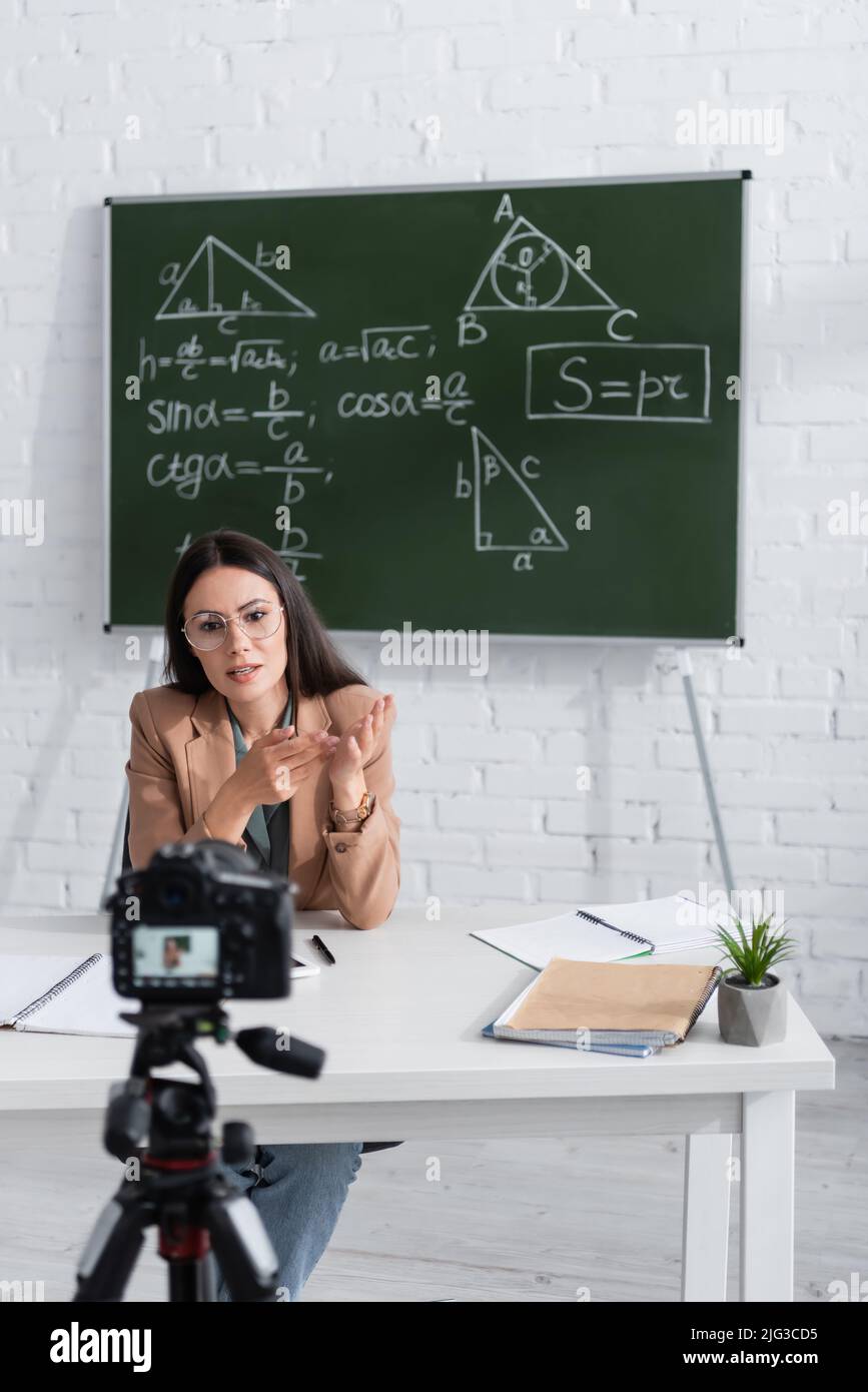 Teacher talking near digital camera and chalkboard with math formulas ...