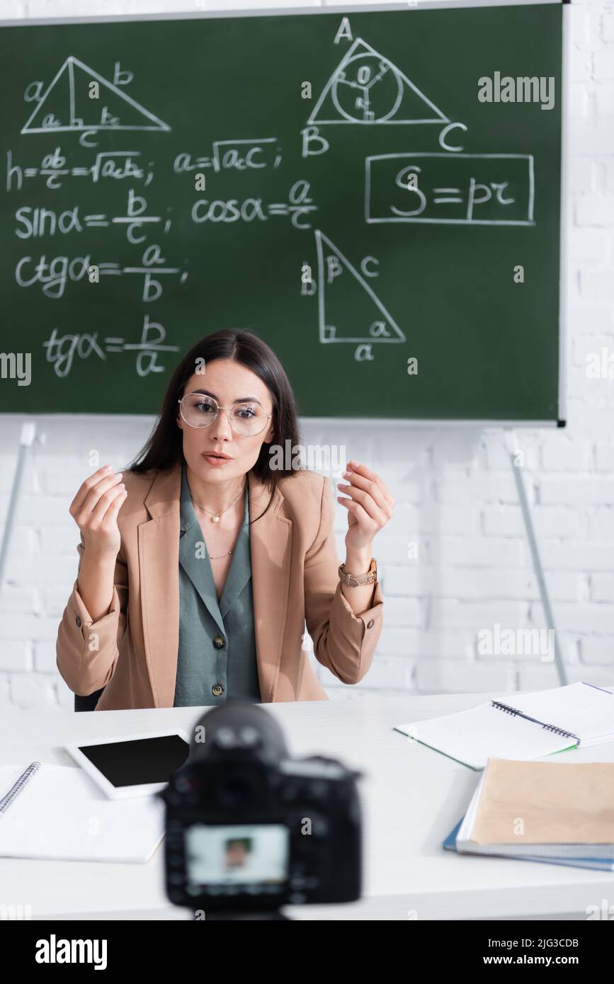Teacher talking near blurred digital camera and chalkboard with math ...