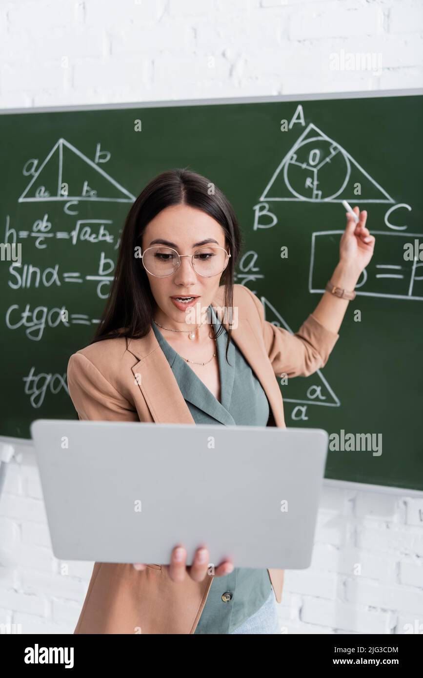 Teacher having video call on laptop near chalkboard with math formulas ...