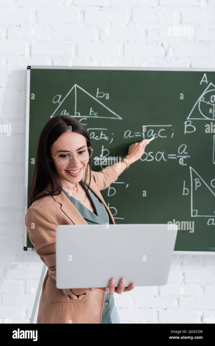 Teacher pointing at math formulas on chalkboard during online lesson in ...