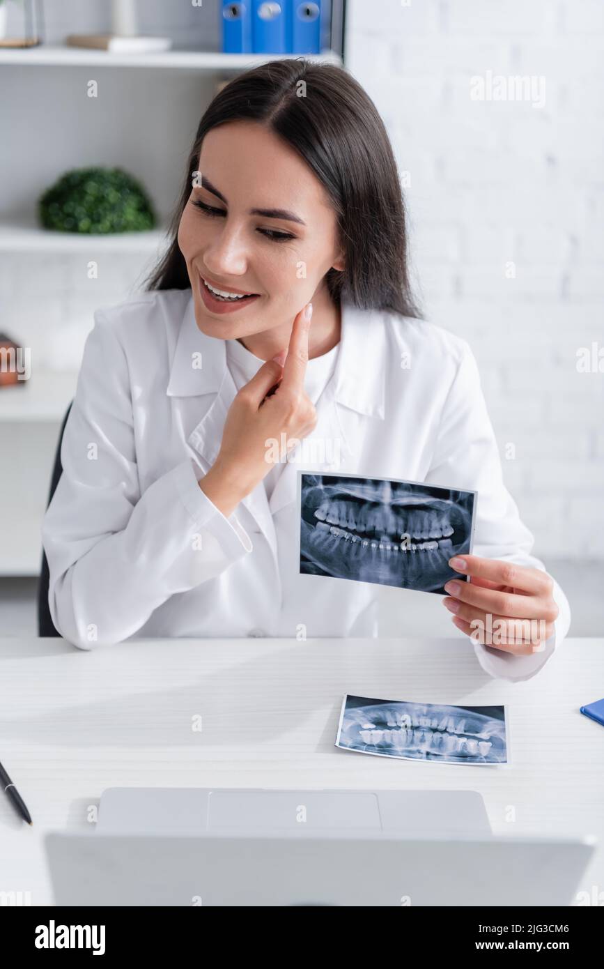 Positive doctor holding scan of teeth and pointing at cheek during ...