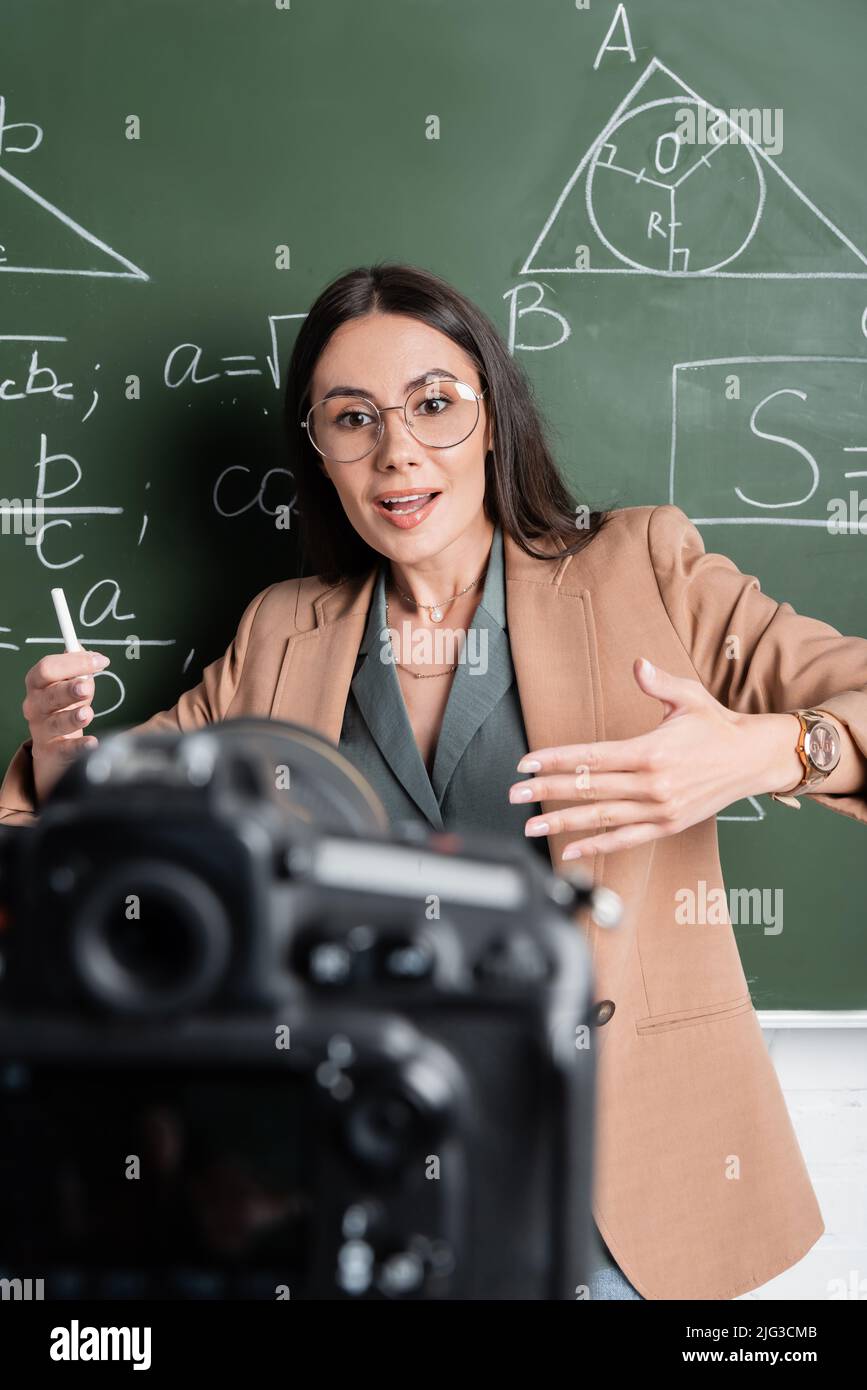 Teacher talking near math formulas on chalkboard and blurred digital ...