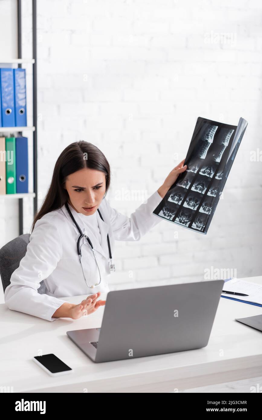 Doctor holding mri scan during online consultation on laptop in clinic ...