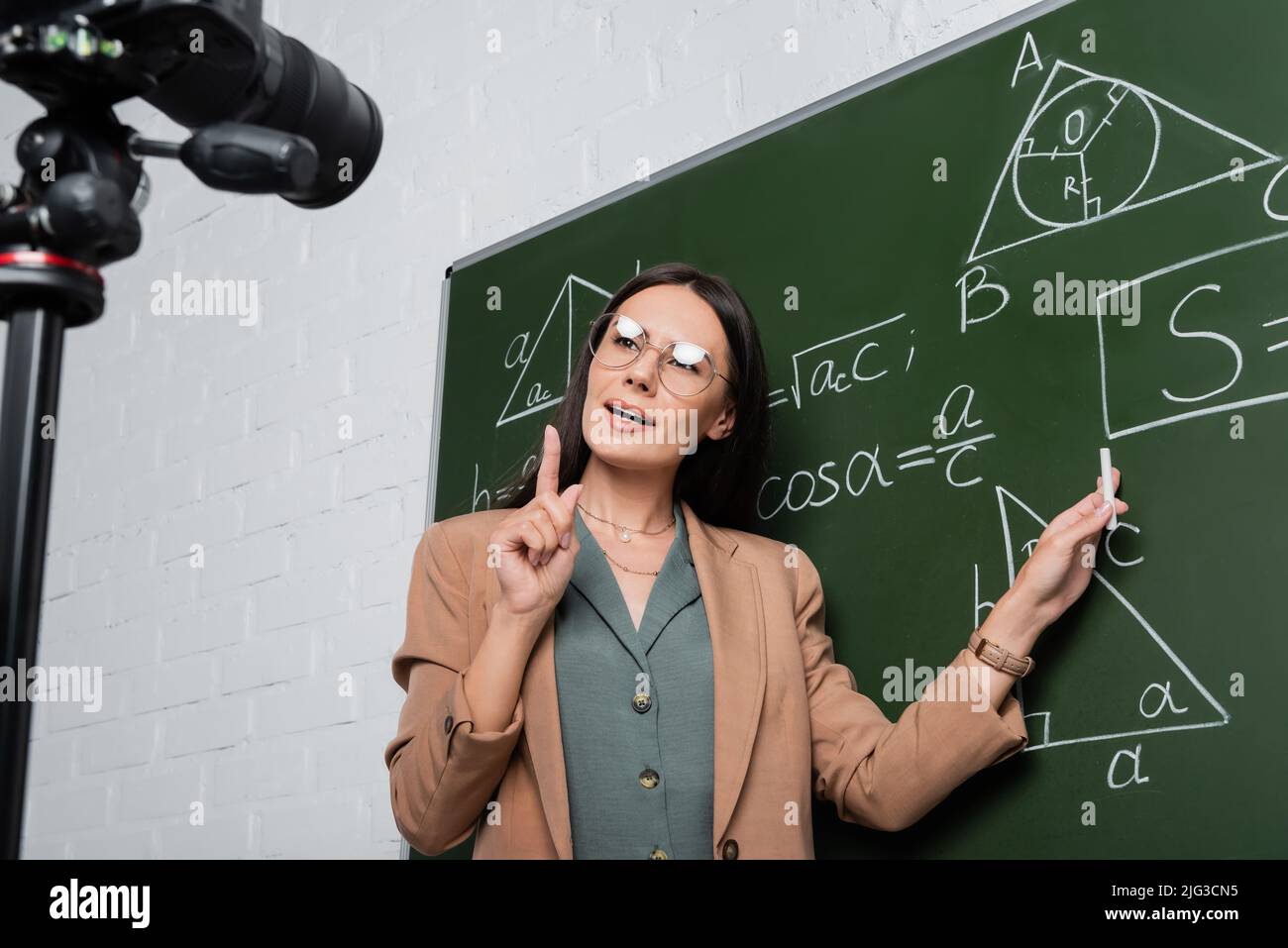 Teacher in eyeglasses explaining math formulas on chalkboard near ...