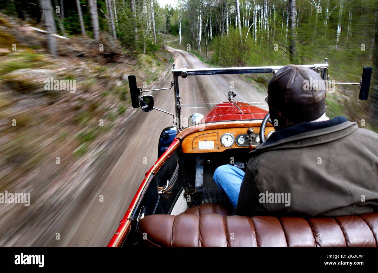 Someone driving an old Fiat from 1925, on a gravel road in a forest ...