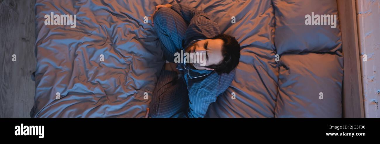 Overhead view of man with closed eyes sitting on bed at home, banner ...