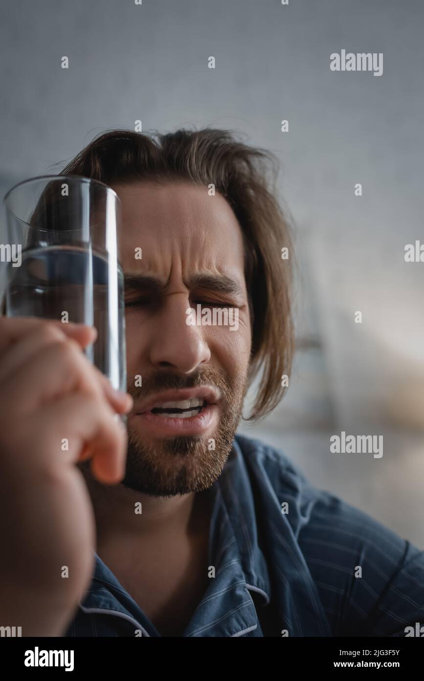 Exhausted man holding glass of water while suffering from insomnia at ...