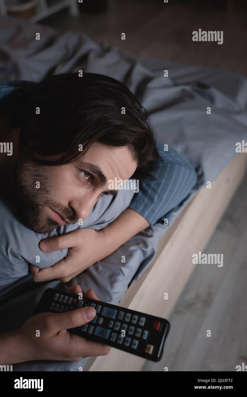 Sleepless man holding remote controller while lying on pillow in ...