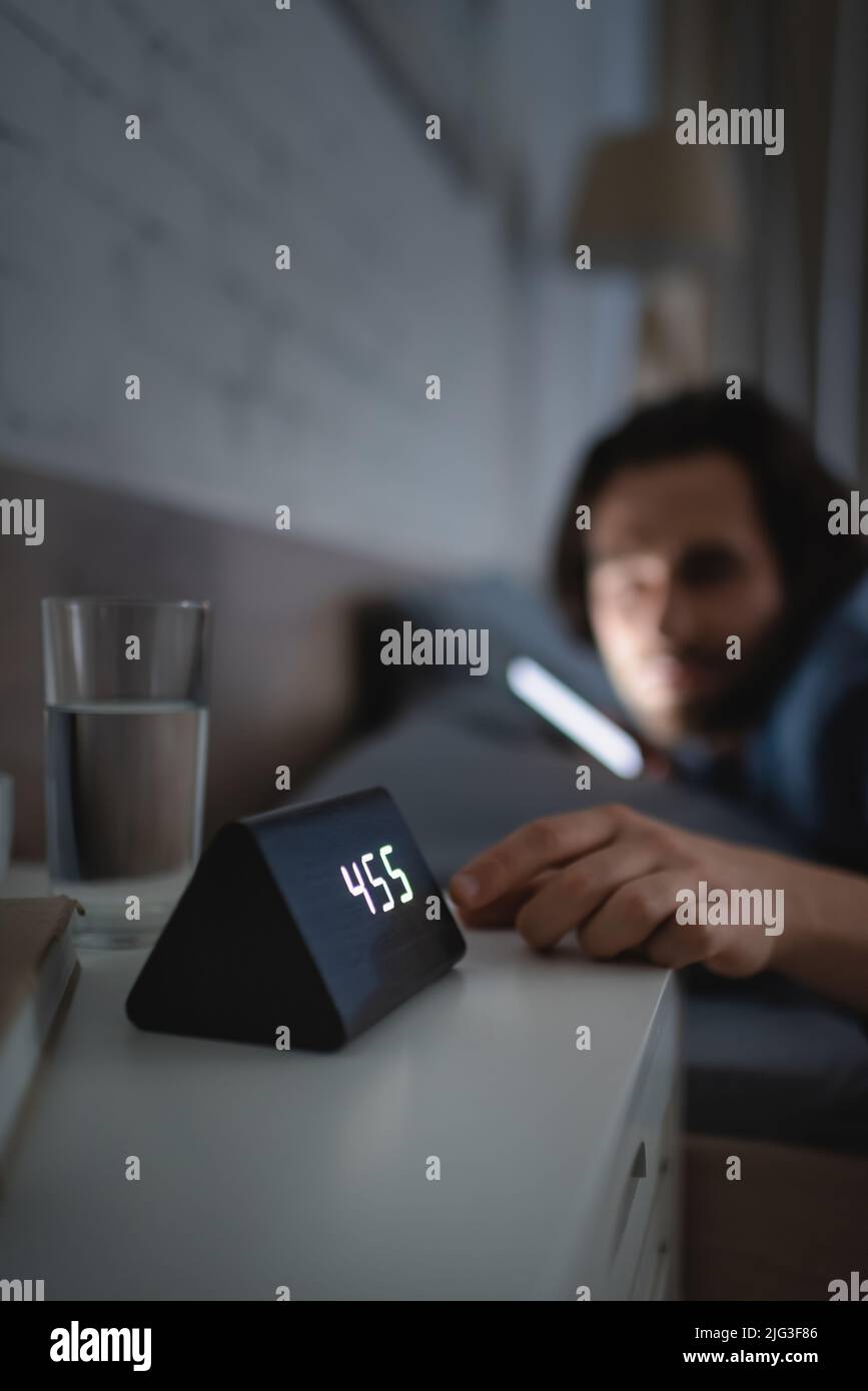 Blurred man touching alarm clock on bedside table at night Stock Photo ...