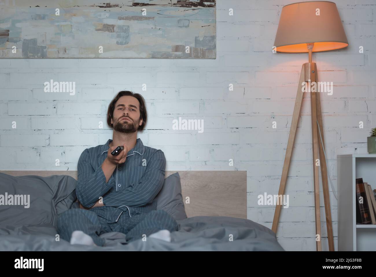 Bearded man with sleep disorder clicking channels while sitting on bed ...