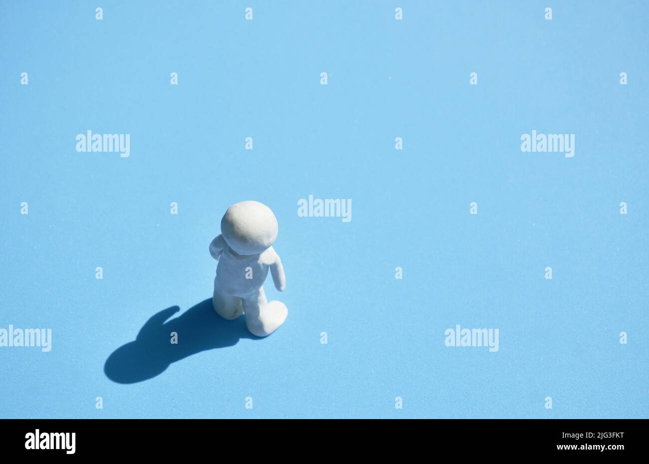 white clay man standing on sunlight with shadow on blue background ...