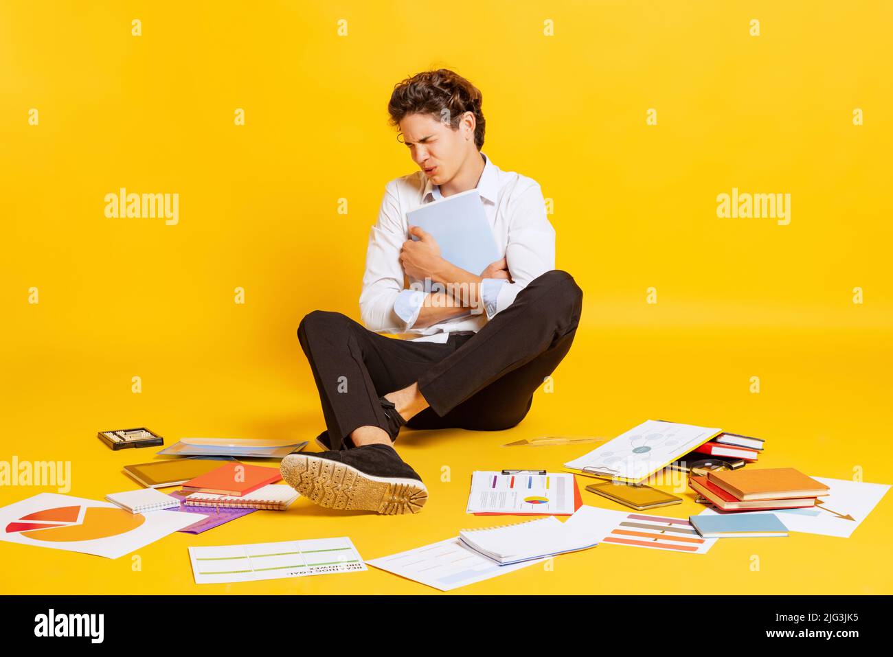 Young annoyed boy, teen in business style clothes sitting on floor and ...
