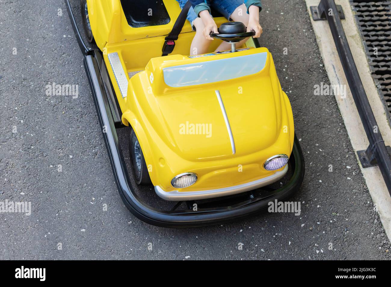 Children's hands hold the steering wheel of a miniature yellow car ...